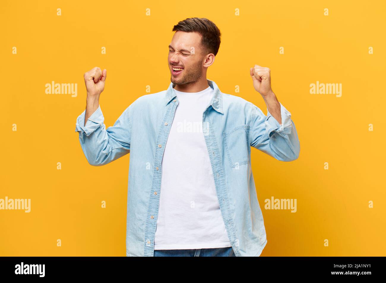 Lucky smiling tanned handsome man in blue basic t-shirt raise fist up ...