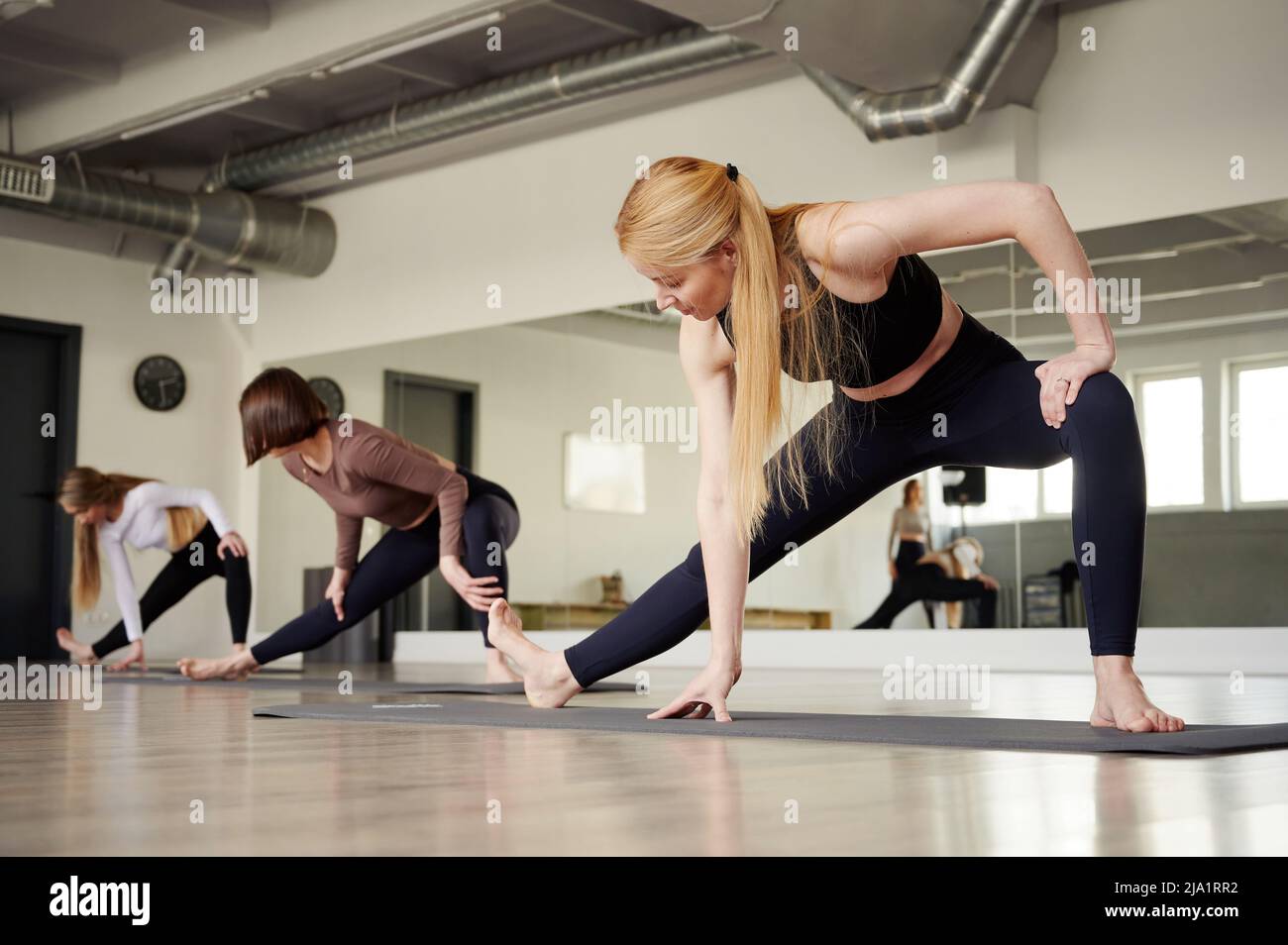 Group of women stretching legs at yoga class in fitness studio ...