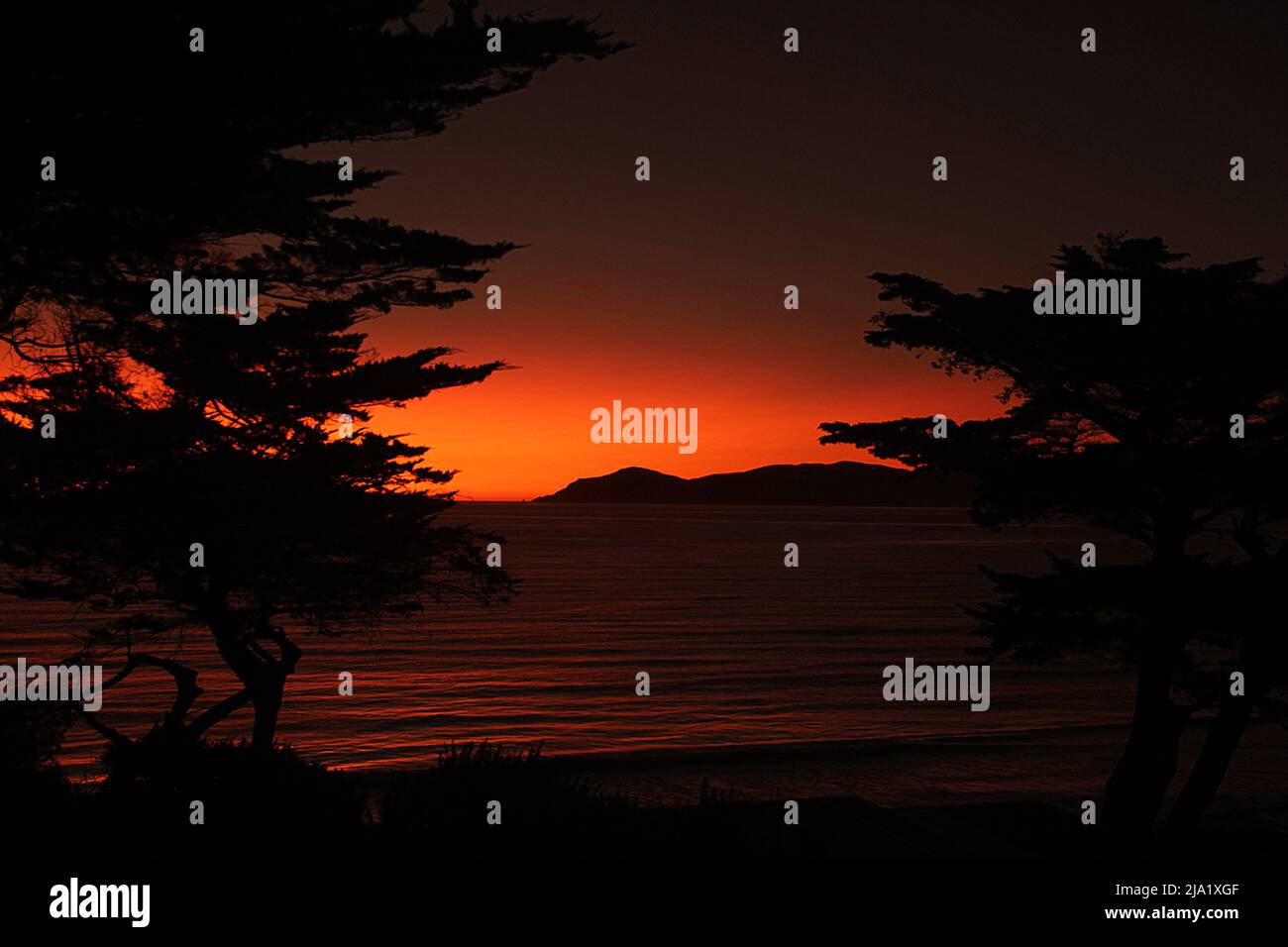 Fiery red sunset silouetting trees and island Stock Photo - Alamy