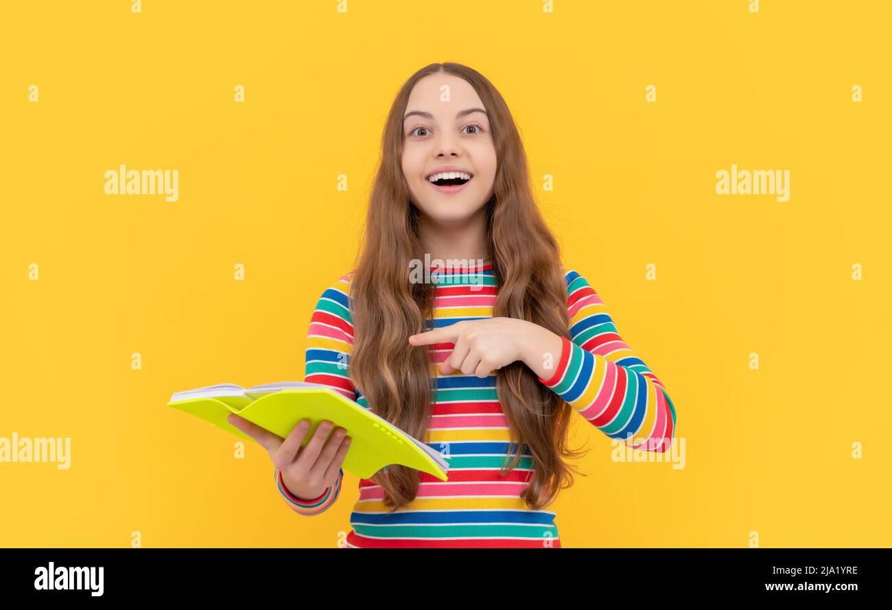 Happy kid smile pointing finger at school book yellow background, study ...