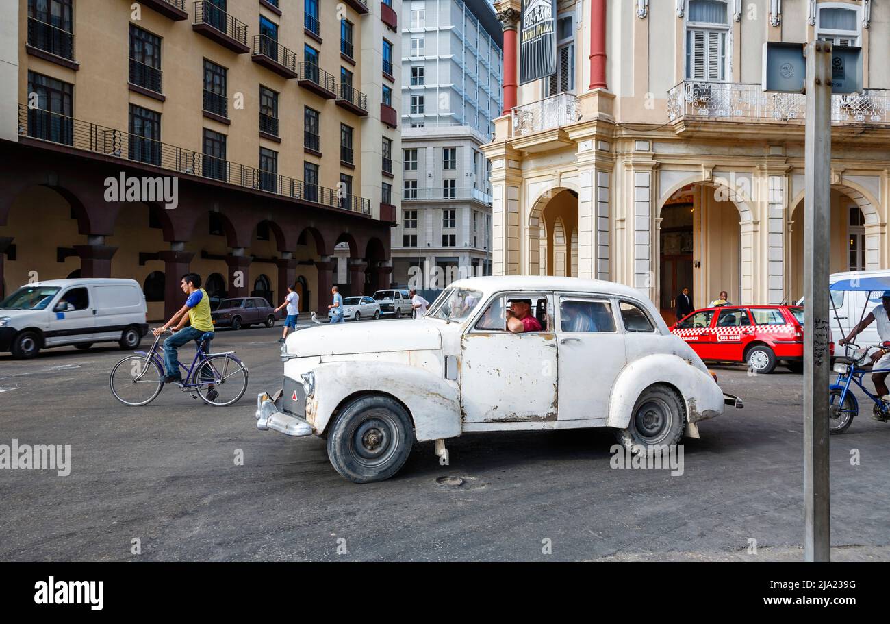 A battered, dilapidated, rusting vintage white American car is driven ...