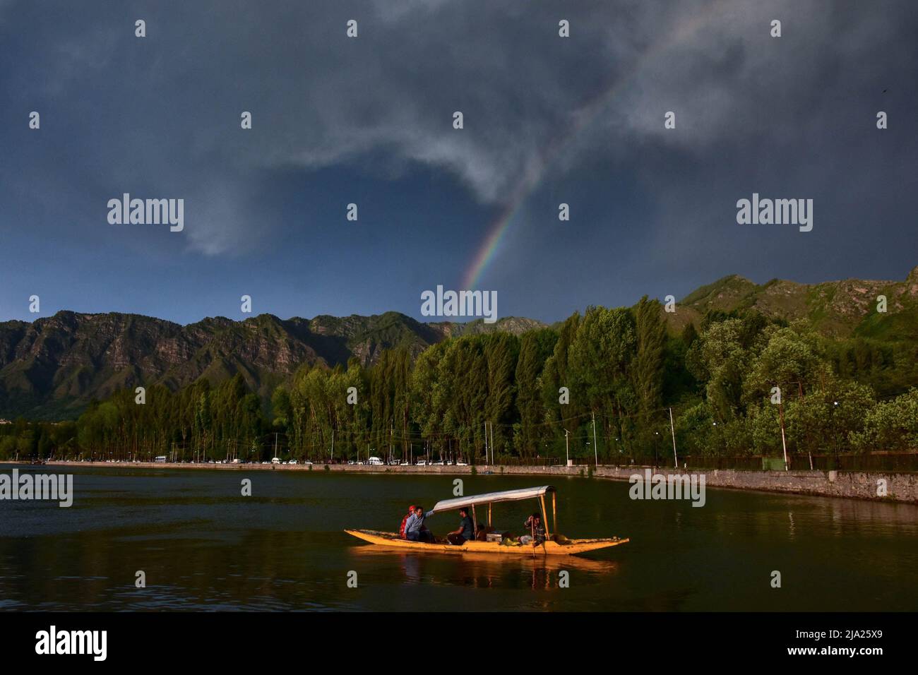 A rainbow is seen as boatmen ferry tourists across the Dal lake on a ...