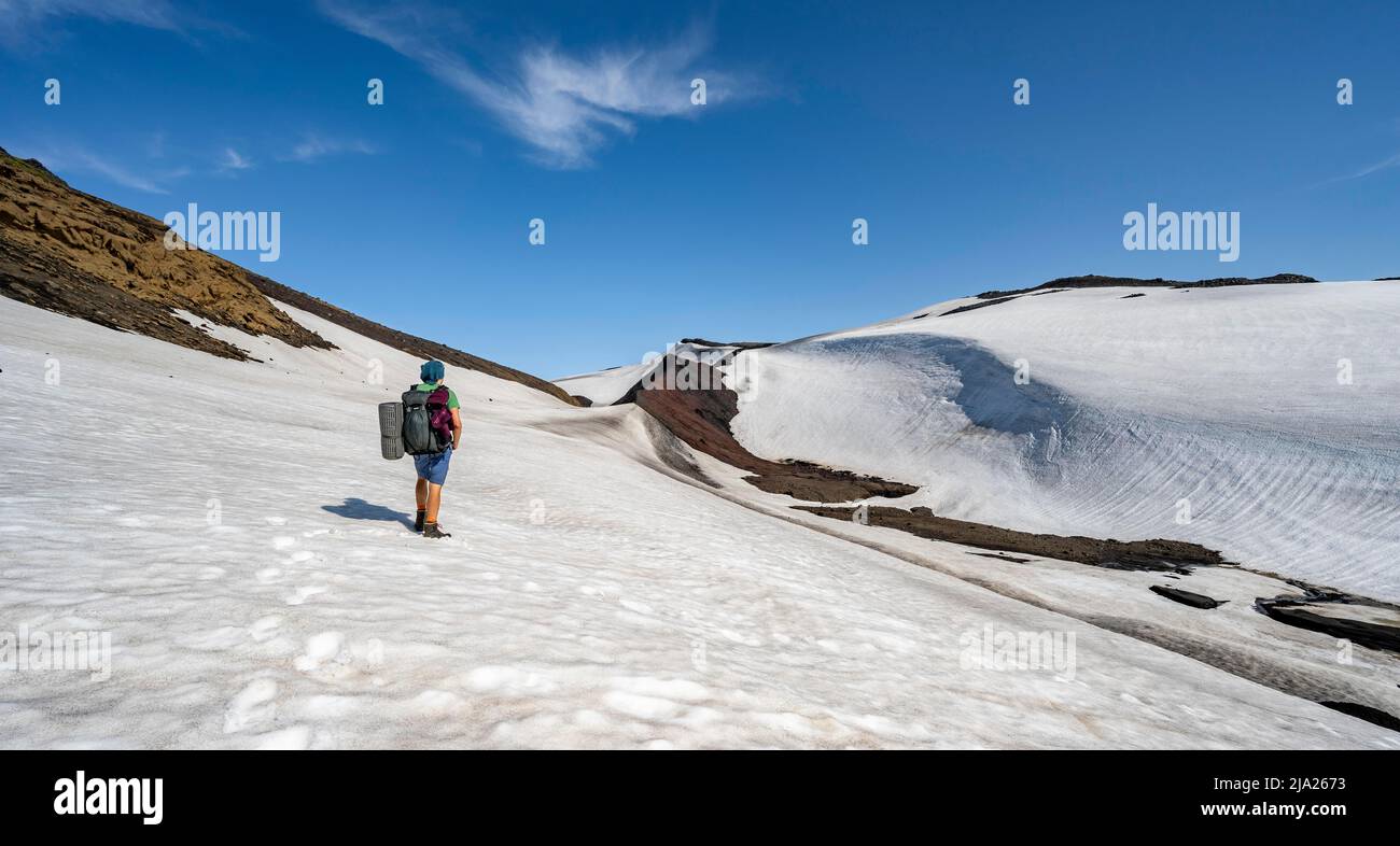 Hikers on the Fimmvoerouhals trail on a snowfield, barren volcanic ...