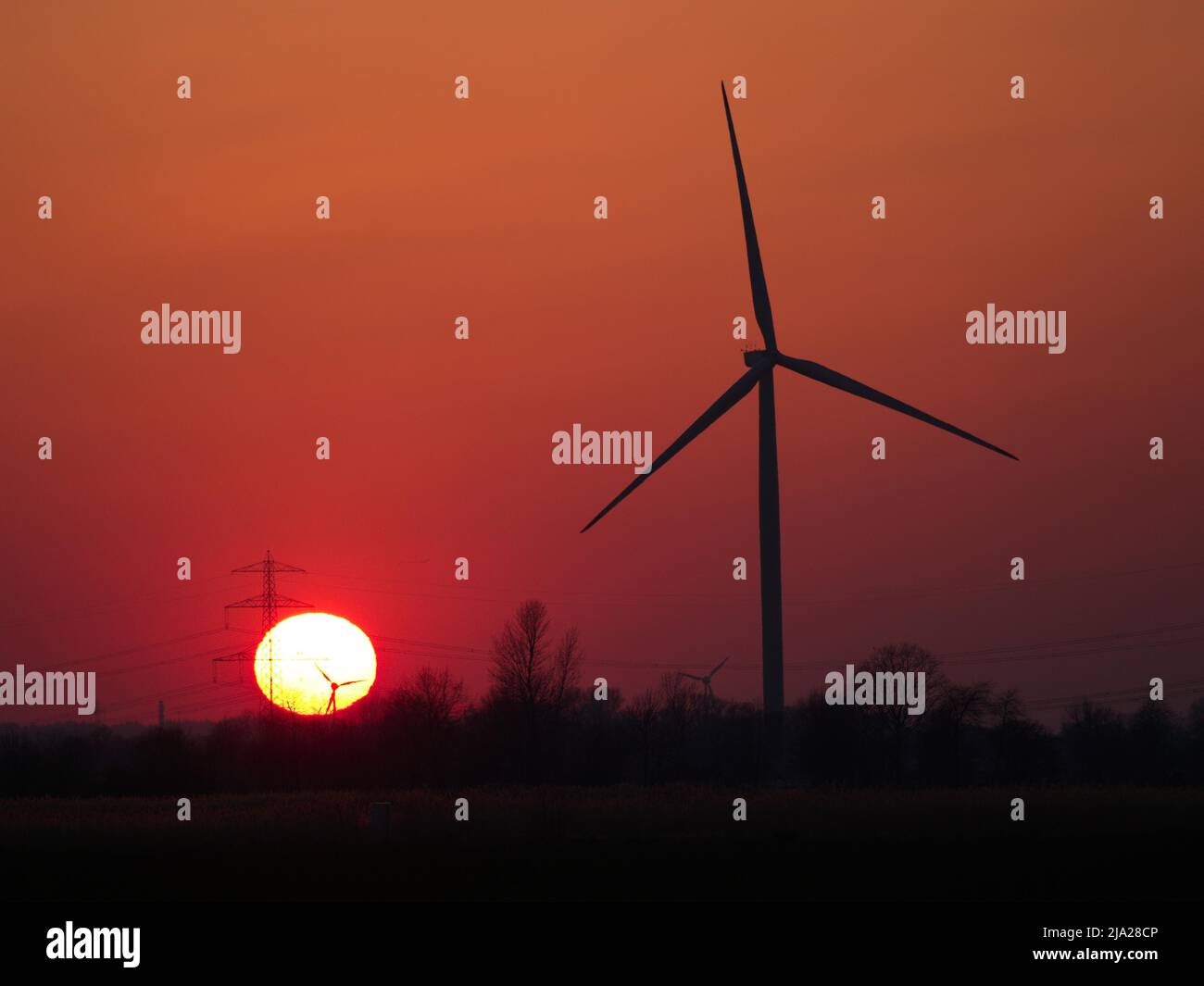 Wind turbine and high-voltage line in front of the setting sun in ...