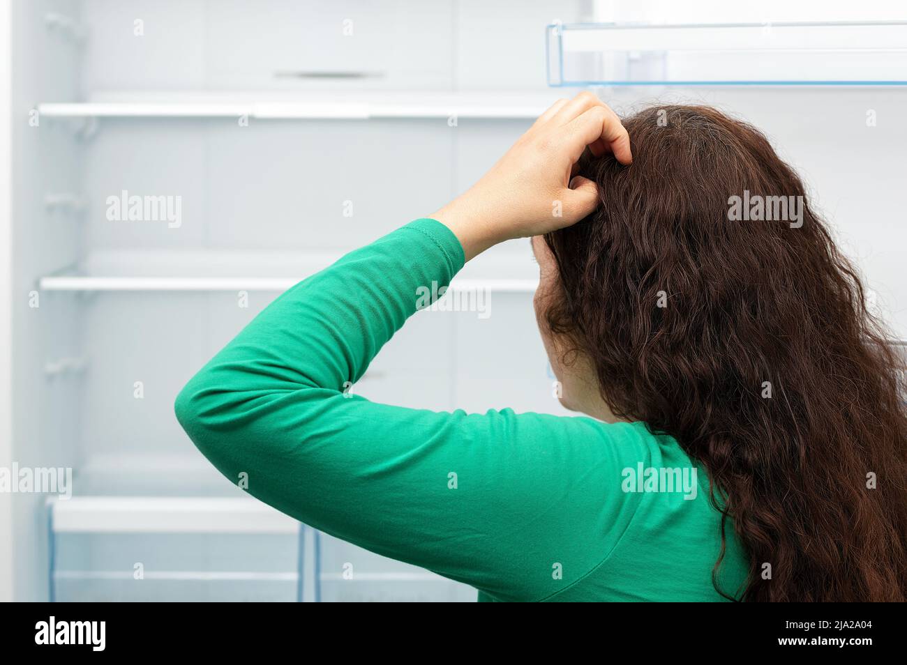 Rearview of a young woman looking in her empty fridge with copy space ...