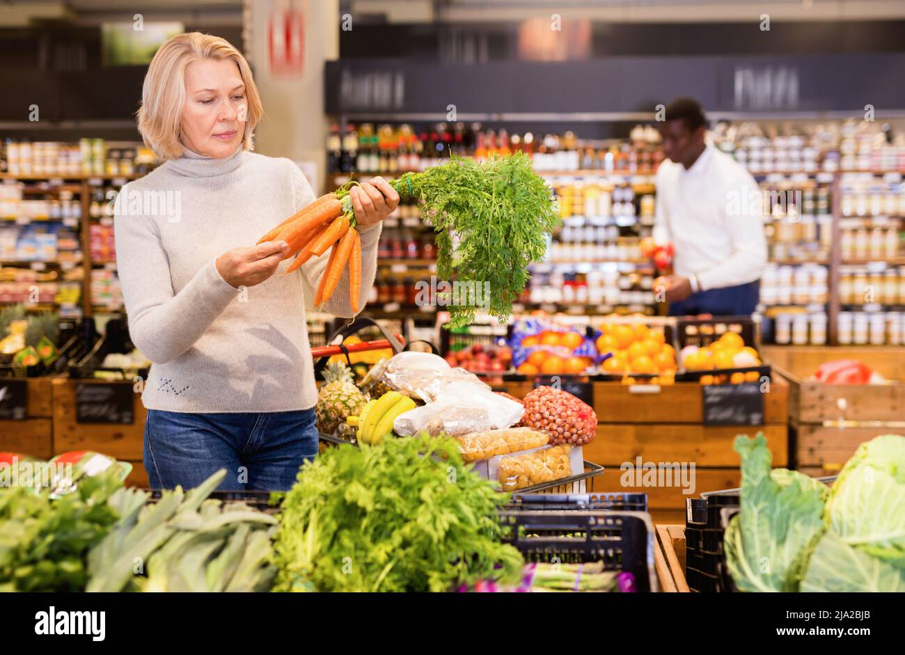 Focused middle aged woman shopping in organic food store, choosing ...