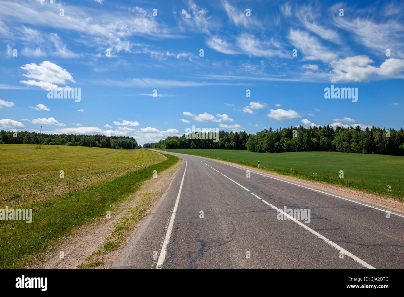 paved highway with blue sky and clouds, a highway through a field with ...