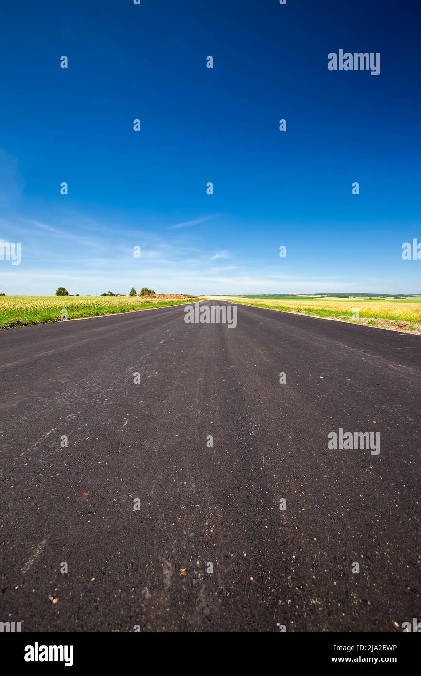 an asphalt road with a blue cloudless sky , a road through a field with ...