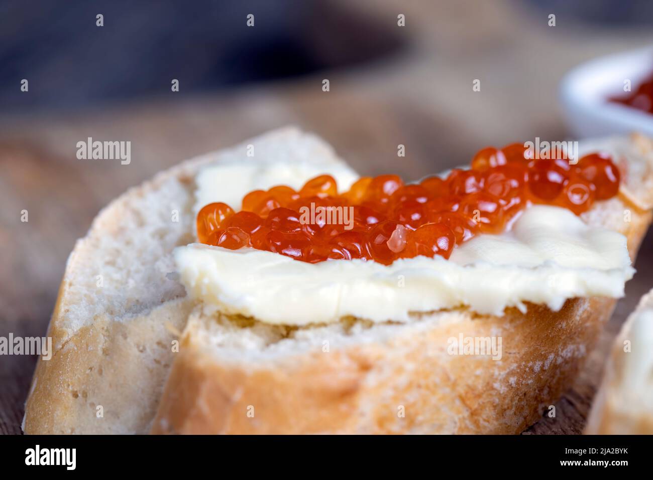 red salmon or trout caviar with white baguette and butter, making ...