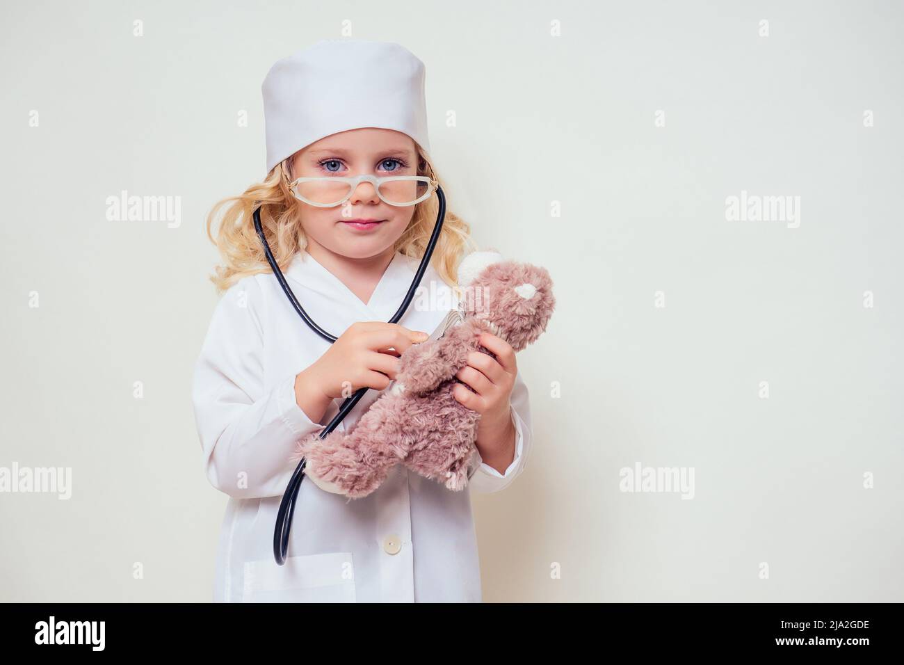 Adorable child girl uniformed wearing doctor's cap and glasses playing ...