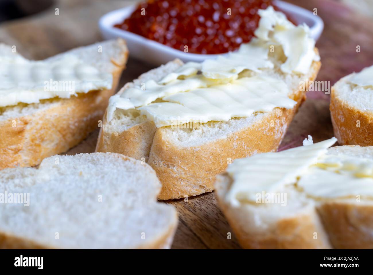 red salmon or trout caviar with white baguette and butter, making ...
