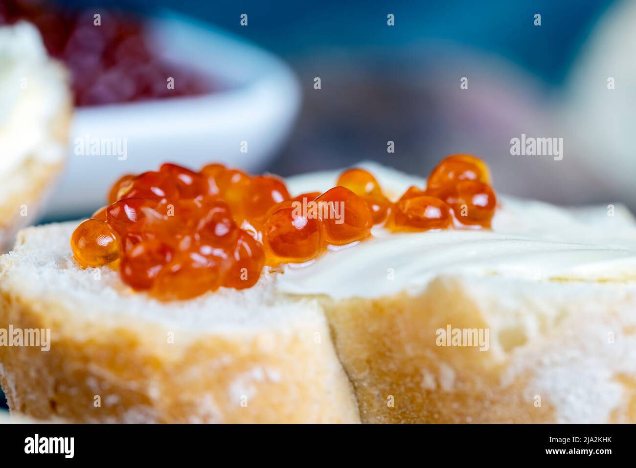 red salmon or trout caviar with white baguette and butter, making ...