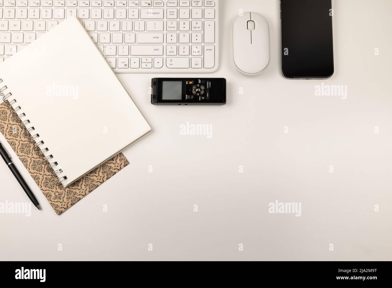 White keyboard, mouse and notepad with black pen and voice recorder ...