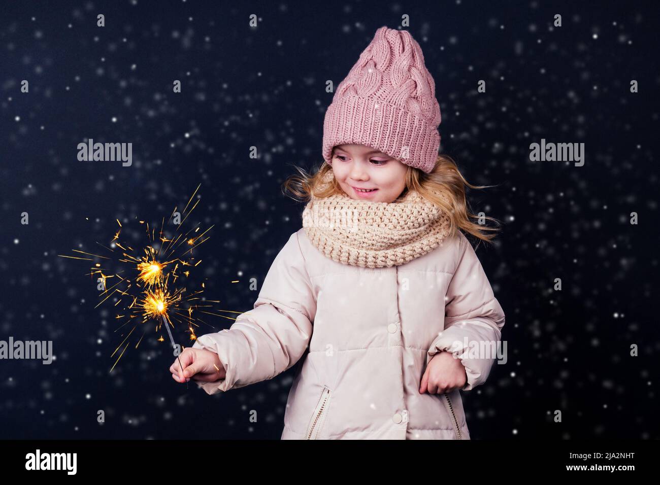 charming little girl in a knitted pink hat holding fireworks on black ...