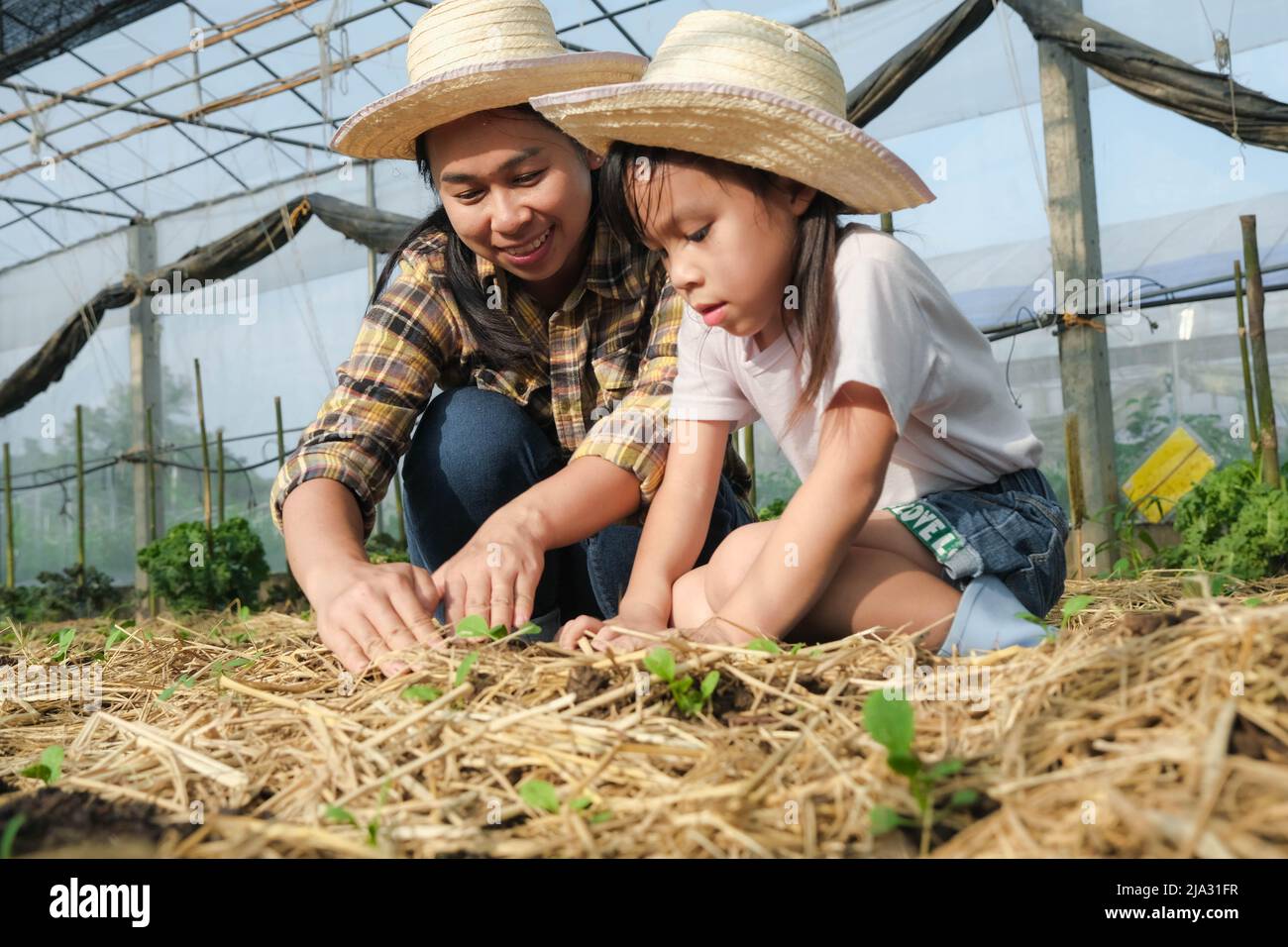 Little girl wearing a hat helps her mother in the garden, a little ...