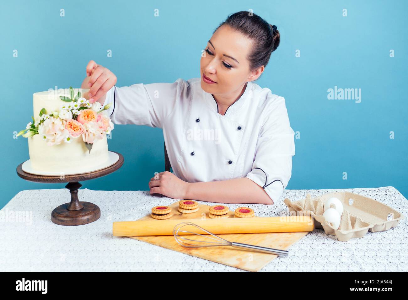 confectioner pastry chef baker woman decorates creamy white two-tiered ...