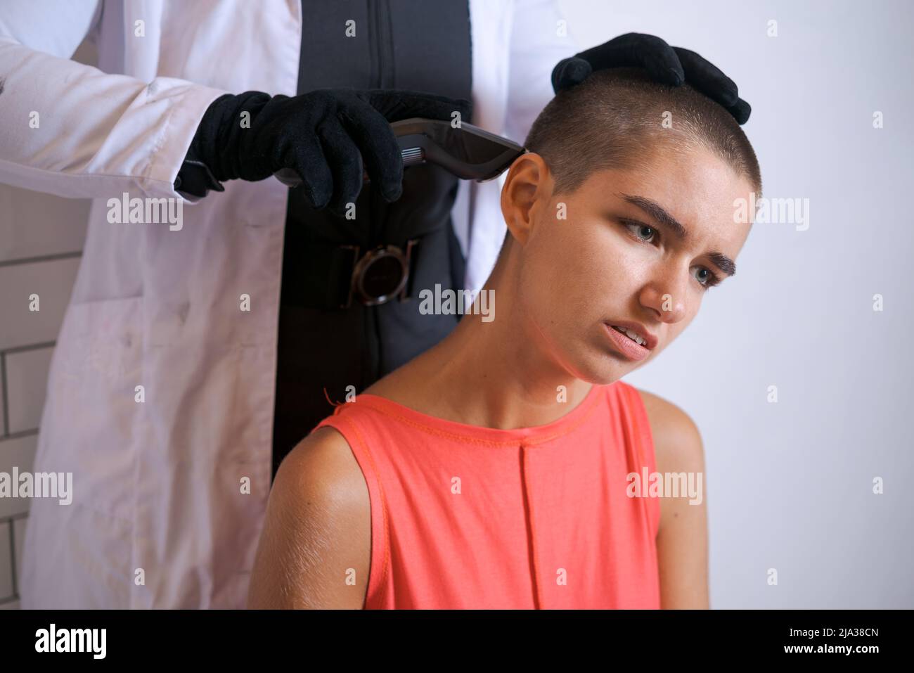 Young woman is forcibly shaving her head with an electric razor ...