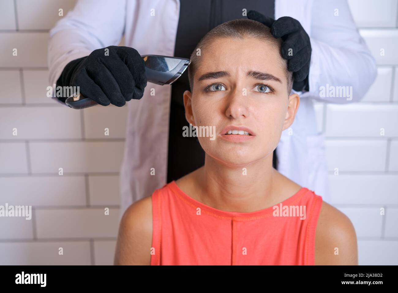 Young woman is forcibly shaving her head with an electric razor ...