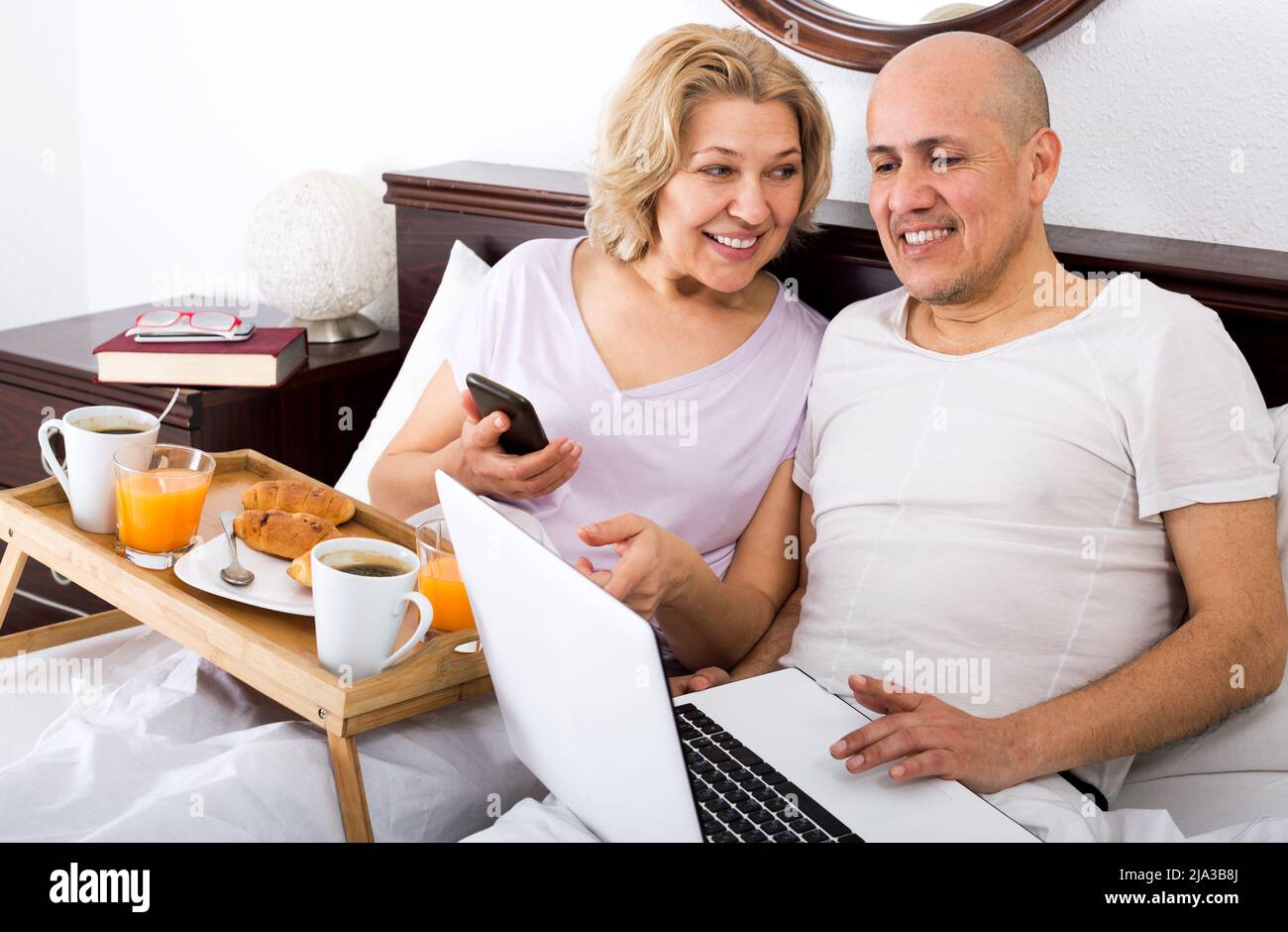 Couple posing with breakfast and laptop in bed Stock Photo - Alamy