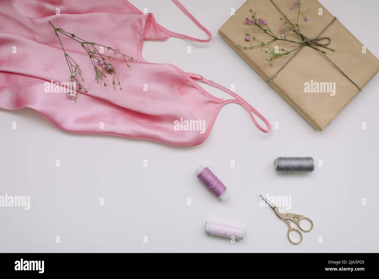 Composition with pink silk fabric, gift in craft paper and threads and ...