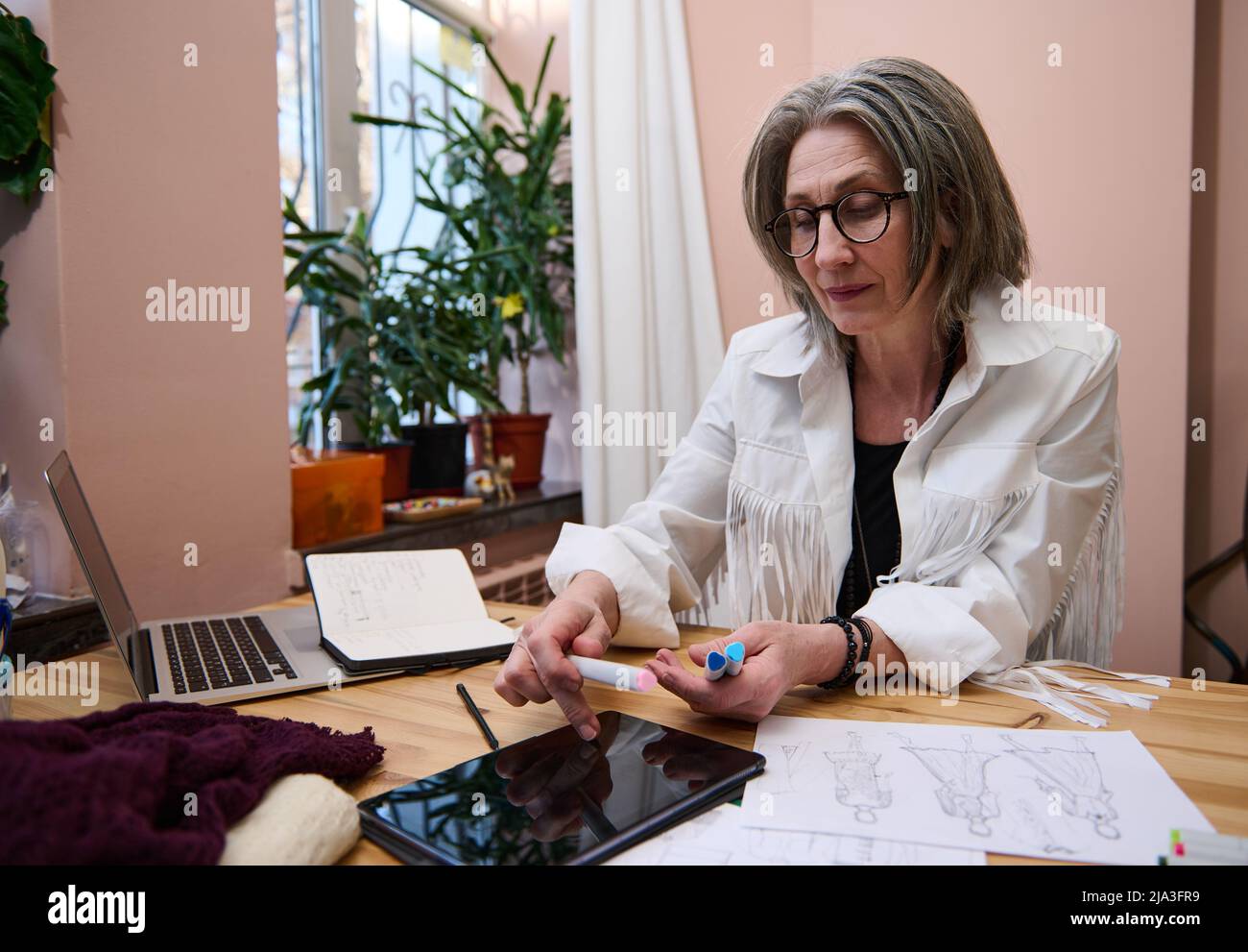 Senior fashion designer tailor holds colorful markers and chooses ...