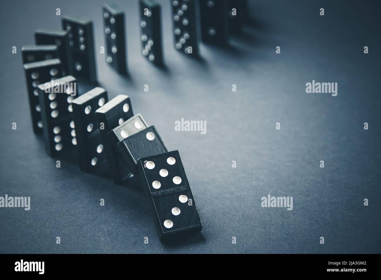 Black dominoes chain on a dark table background. Domino effect concept ...