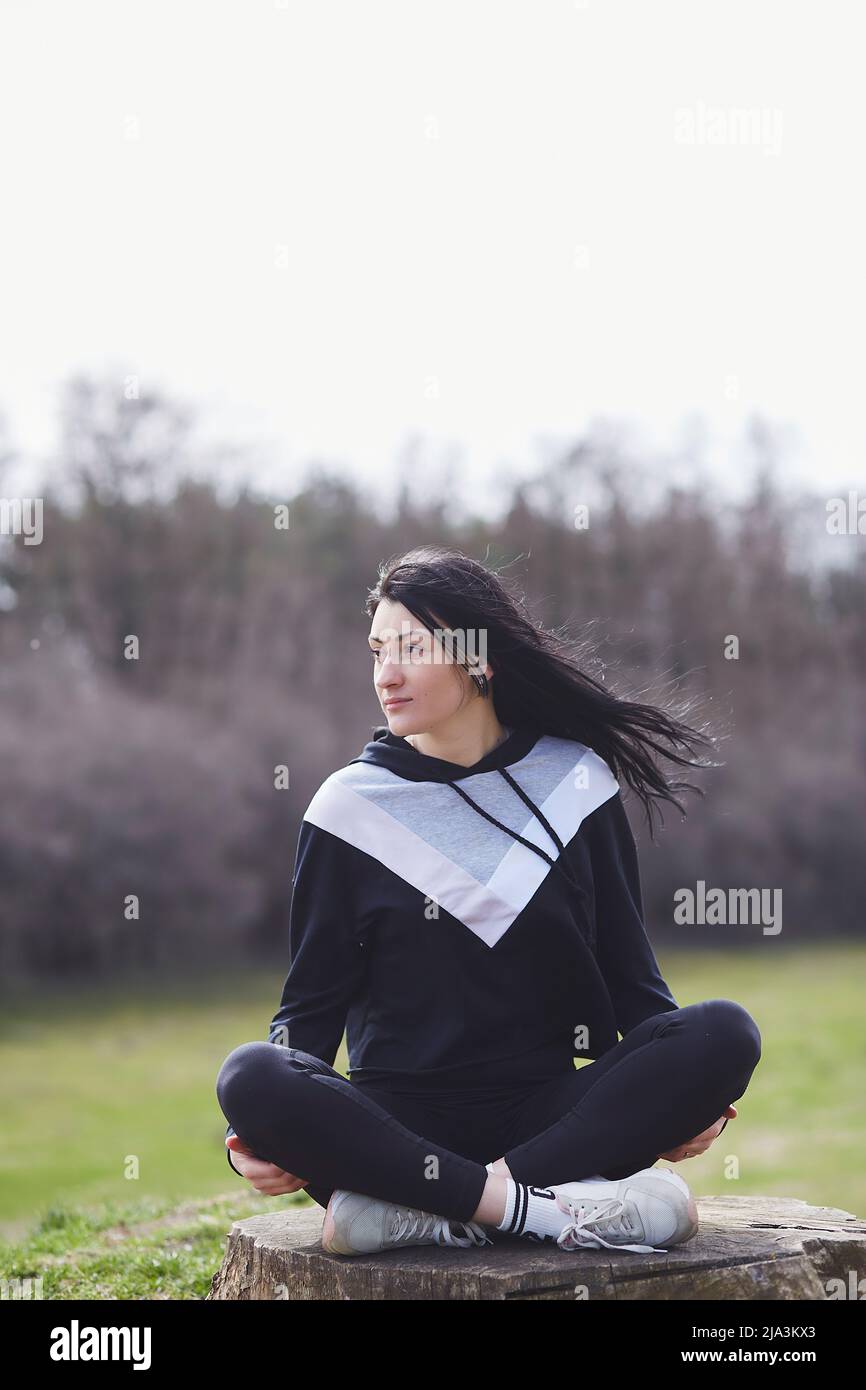 Smiling young woman is sitting in lotus pose on the stump. Meditating ...