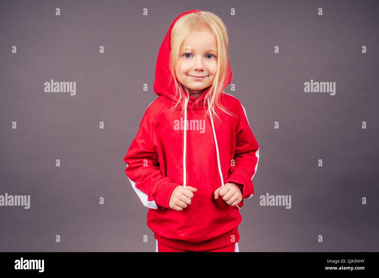 blonde blue-eyed little model girl in a red sports suit posing in the ...