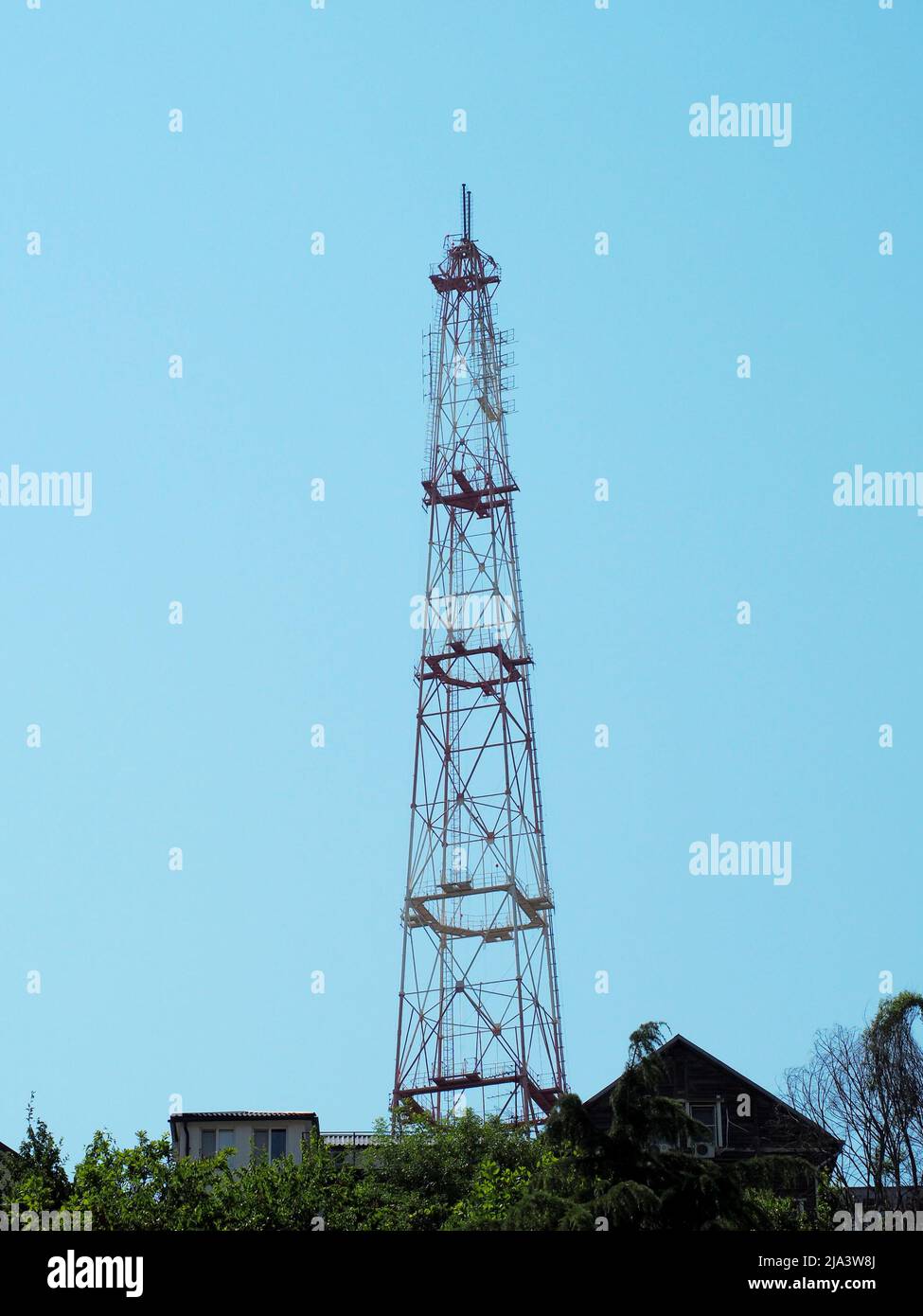 A tall cell tower rises above the rooftops of private houses against ...