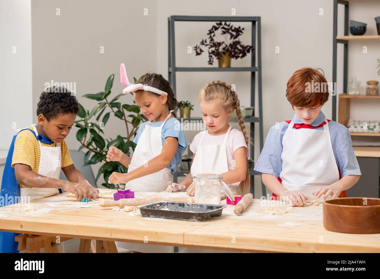 Group of little kids cooking cookies over tray on kitchen table covered ...