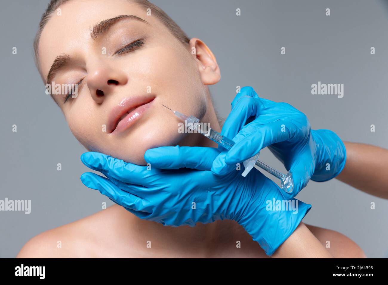 Portrait of young girl doing cosmetology injections isolated over grey ...