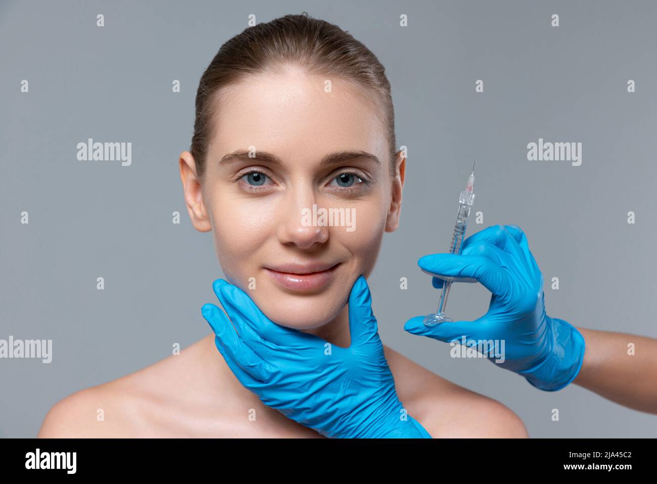 Portrait of young girl doing cosmetology injections isolated over grey ...