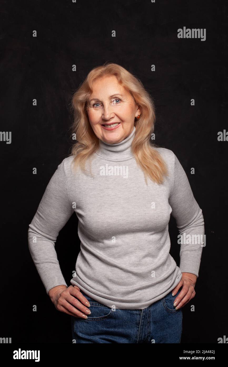 Happy old lady posing indoor. Positive single woman standing on black ...