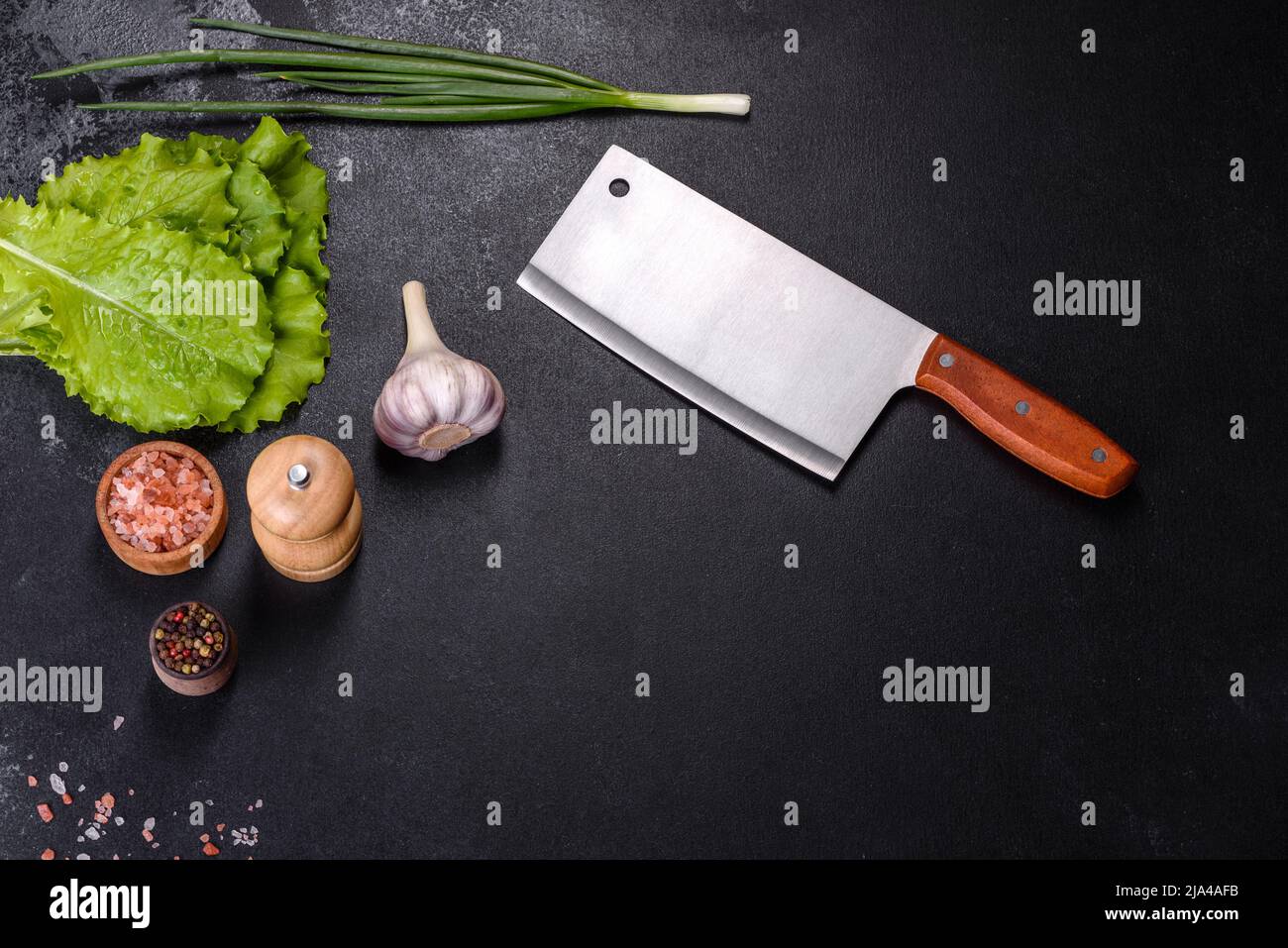 An axe for meat, spices and herbs, a cutting board against a dark ...