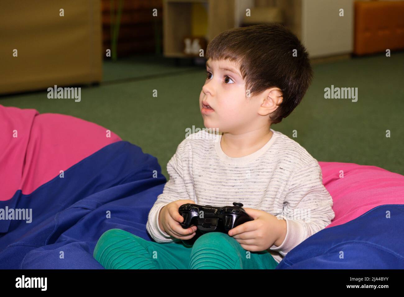 A handsome boy of 4 years old plays a game console, holds a joystick in ...