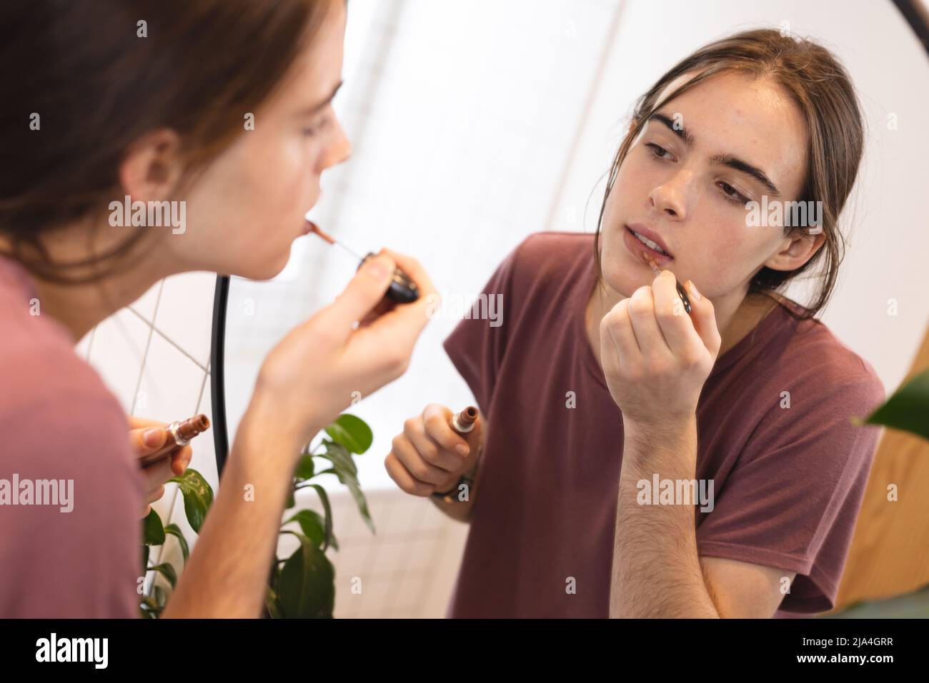 Non-binary trans woman putting lipstick looking in the mirror in ...