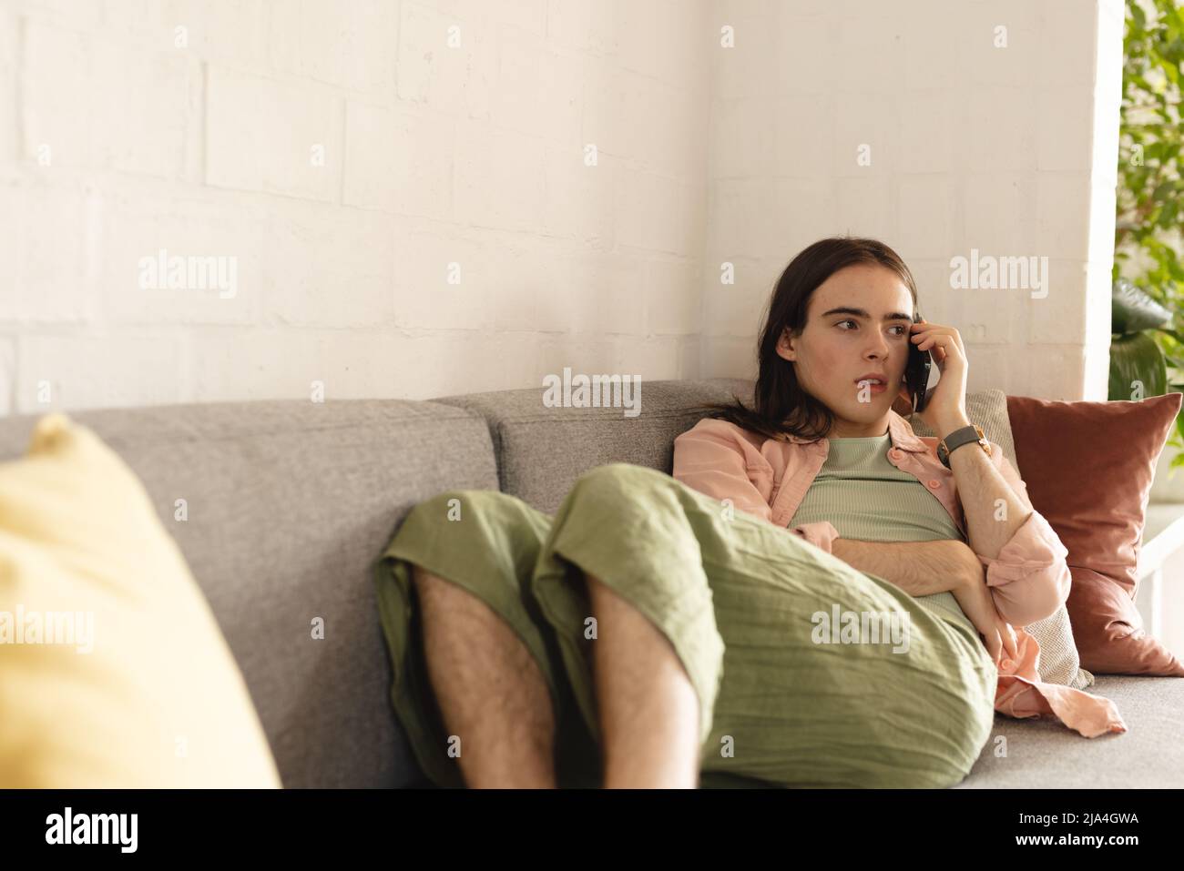 Non-binary trans woman talking on smartphone lying on the couch at home ...