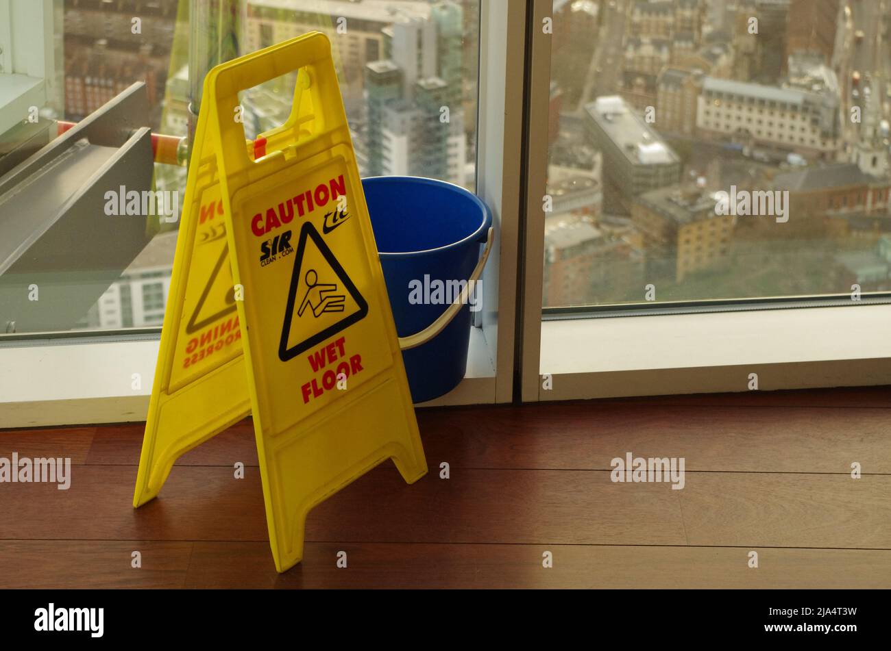Wet floor sign and blue bucket by a window Stock Photo - Alamy