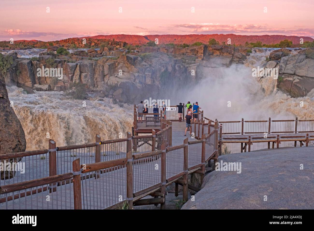 Western tourists watching waterfall from viewing platform at sunset in ...