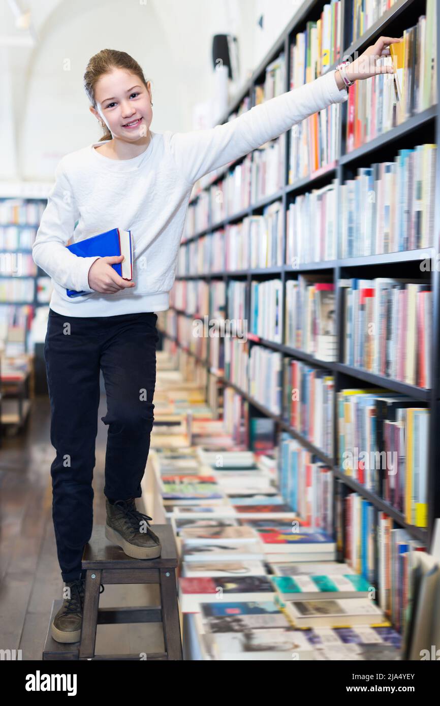 Happy girl on wooden step ladder choosing book Stock Photo - Alamy