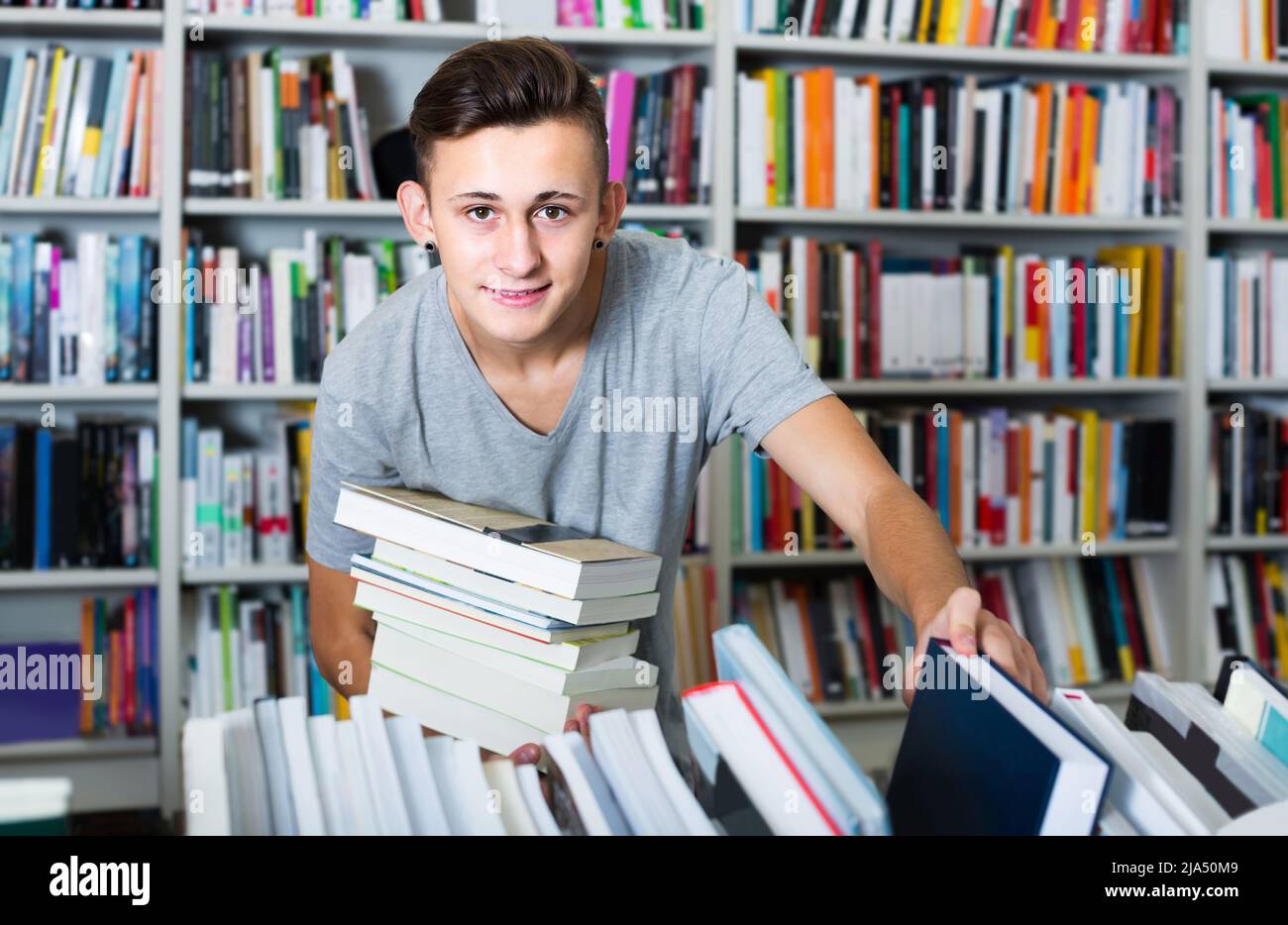portrait of boy standing among bookshelves and searching for book in ...