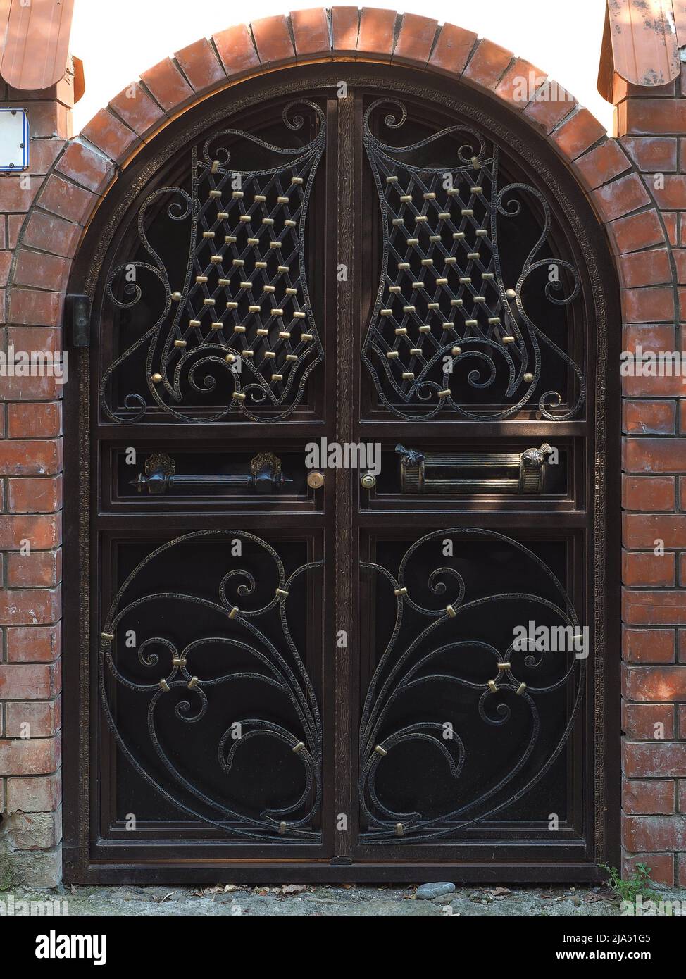 Iron dark gate with gilded pattern next to a brick fence with an arch ...