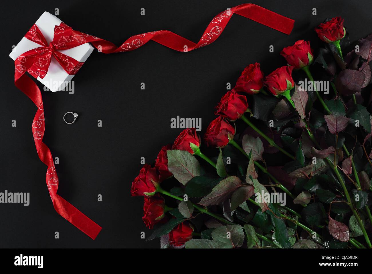 Red roses, ring and gift box on black background Stock Photo - Alamy
