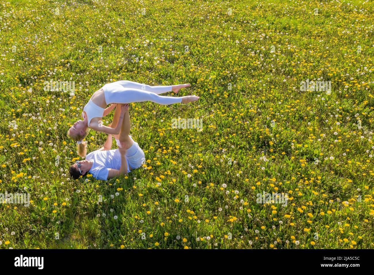 Beautiful young couple doing acro yoga in park. Man lying on grass and ...