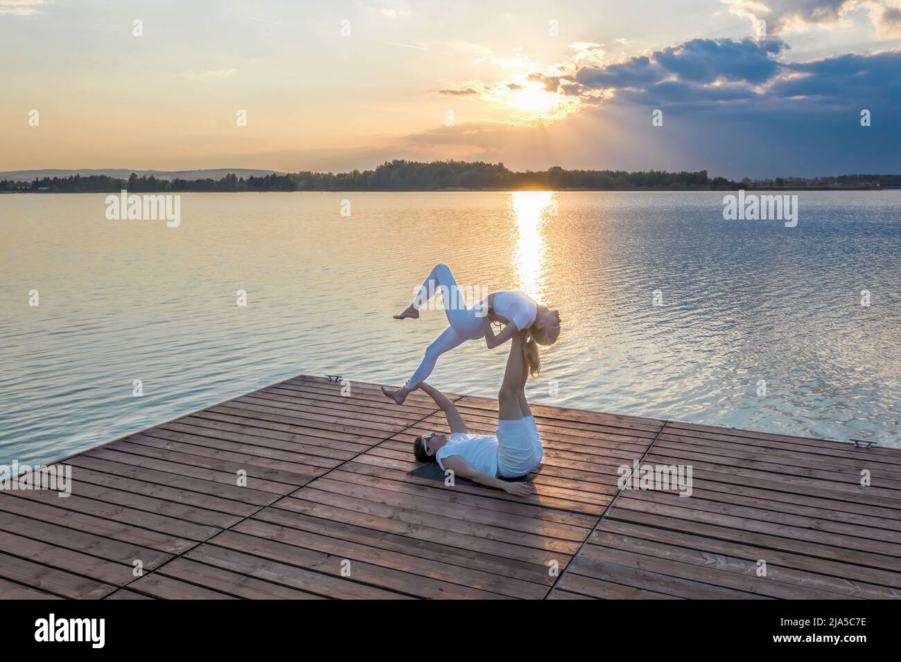 Beautiful young couple doing acro yoga on the pier against sunset. Man ...
