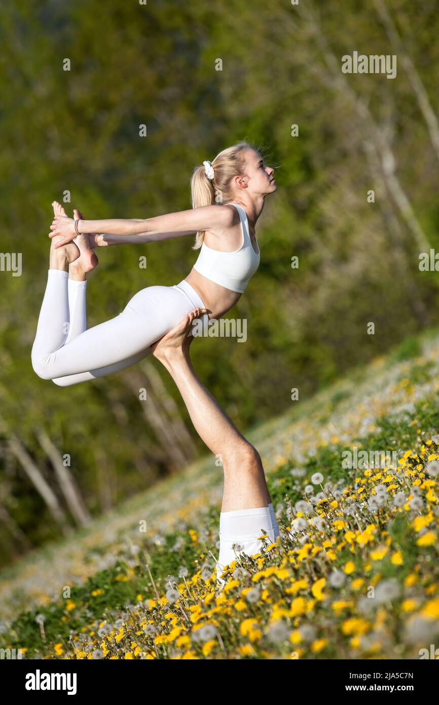 Beautiful young couple doing acro yoga in park. Man lying on grass and ...