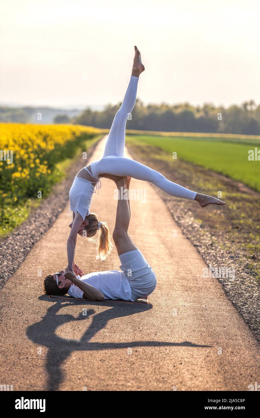 Beautiful young couple doing acro yoga on the bike path. Man lying on road and balancing woman ...