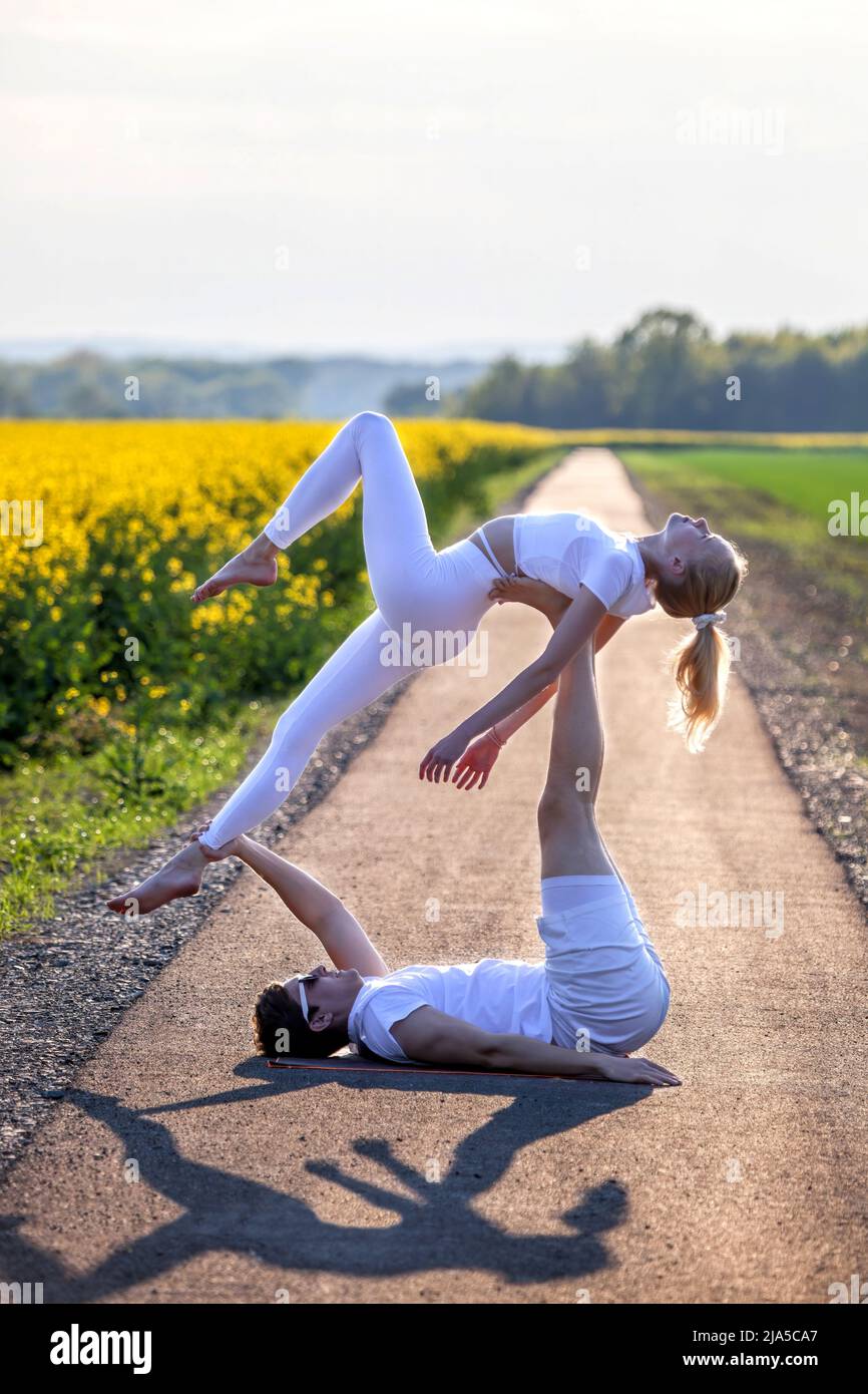 Beautiful young couple doing acro yoga on the bike path. Man lying on ...