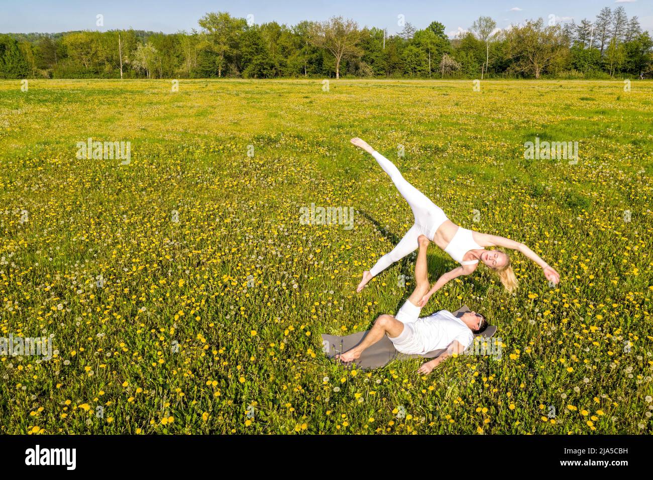 Beautiful young couple doing acro yoga in park. Man lying on grass and ...