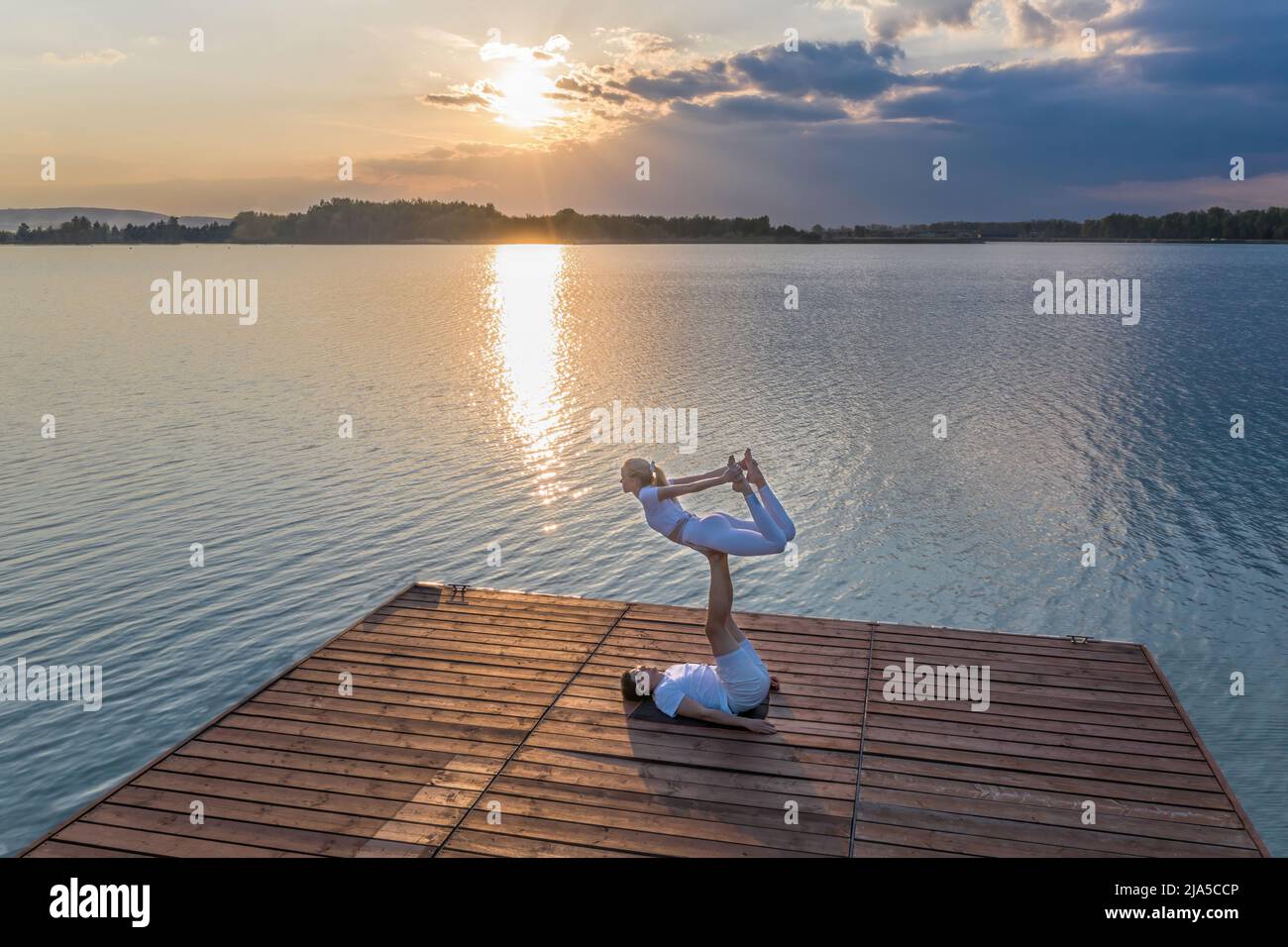 Beautiful young couple doing acro yoga on the pier against sunset. Man ...